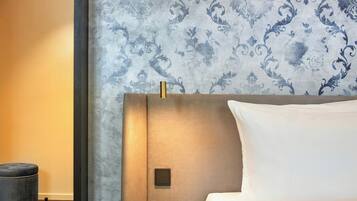 Quarto de hotel com cama, mesa de cabeceira e parede com papel de parede estampado.