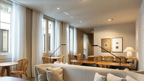 Um hall de hotel moderno com um sofá, mesas de jantar, cadeiras de vime e quadros na parede.