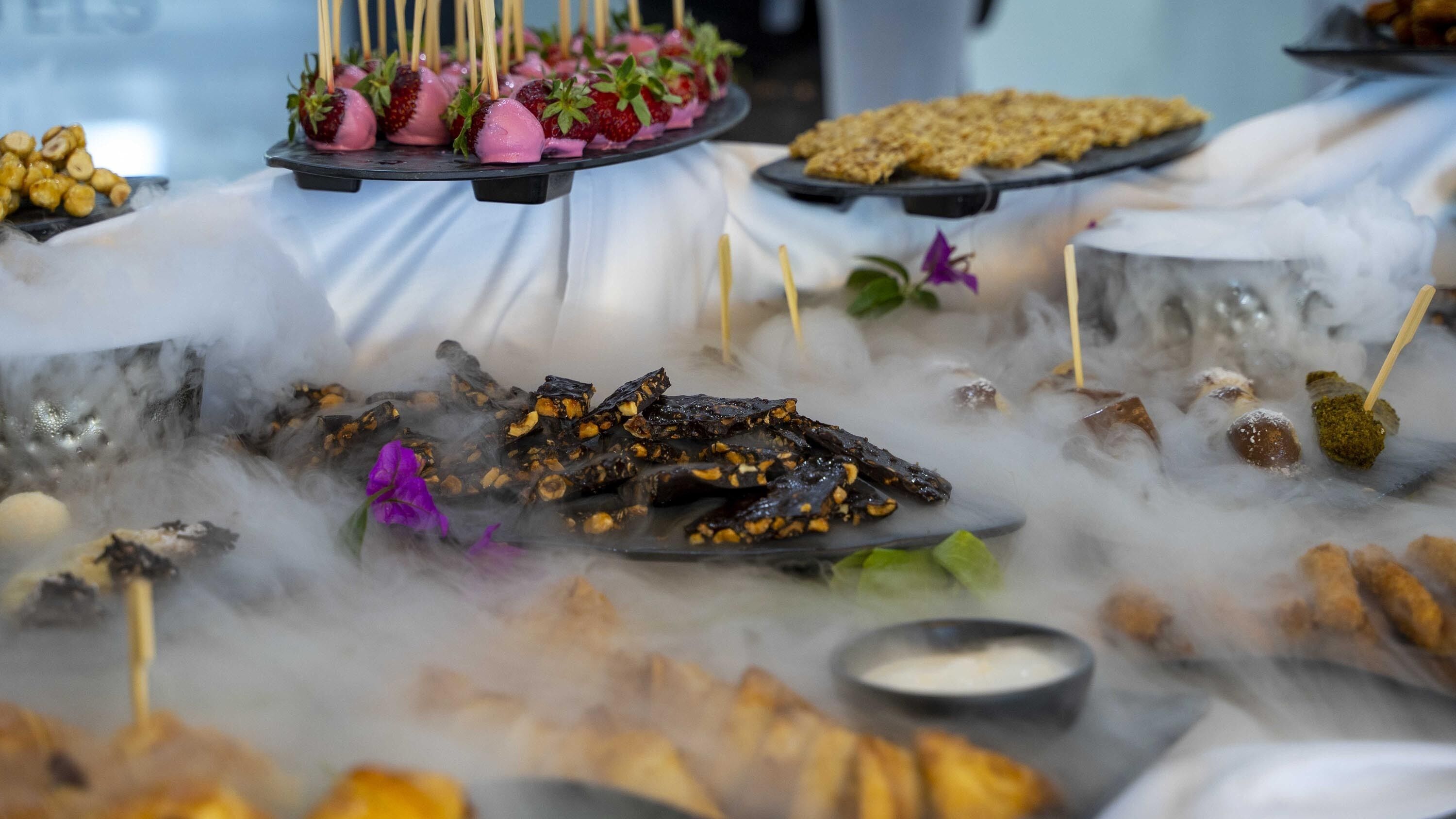 Um buffet com diversos alimentos, incluindo frutas e legumes espetados, e um prato fumegante.