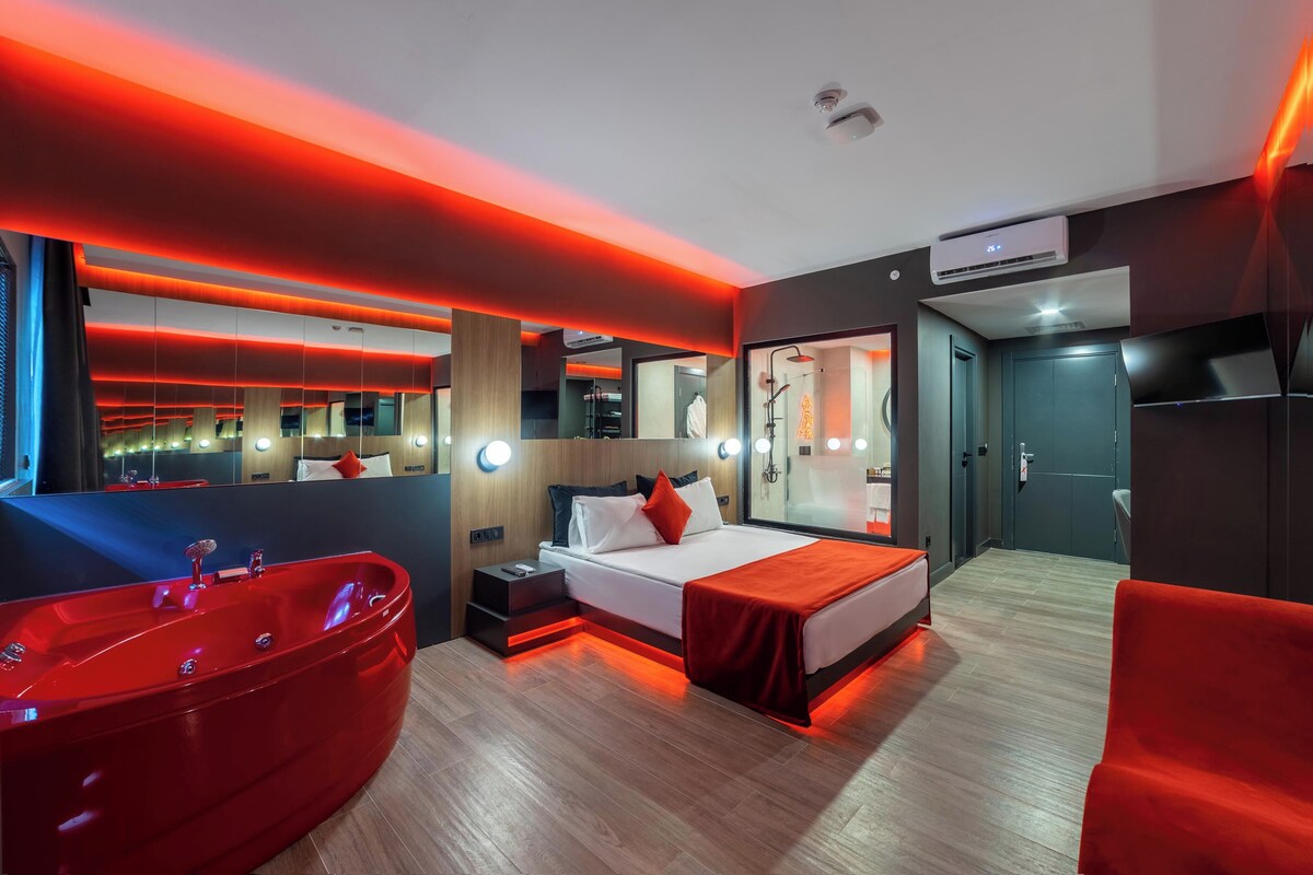 Quarto de hotel moderno com uma cama grande, uma banheira vermelha e um banheiro com chuveiro.