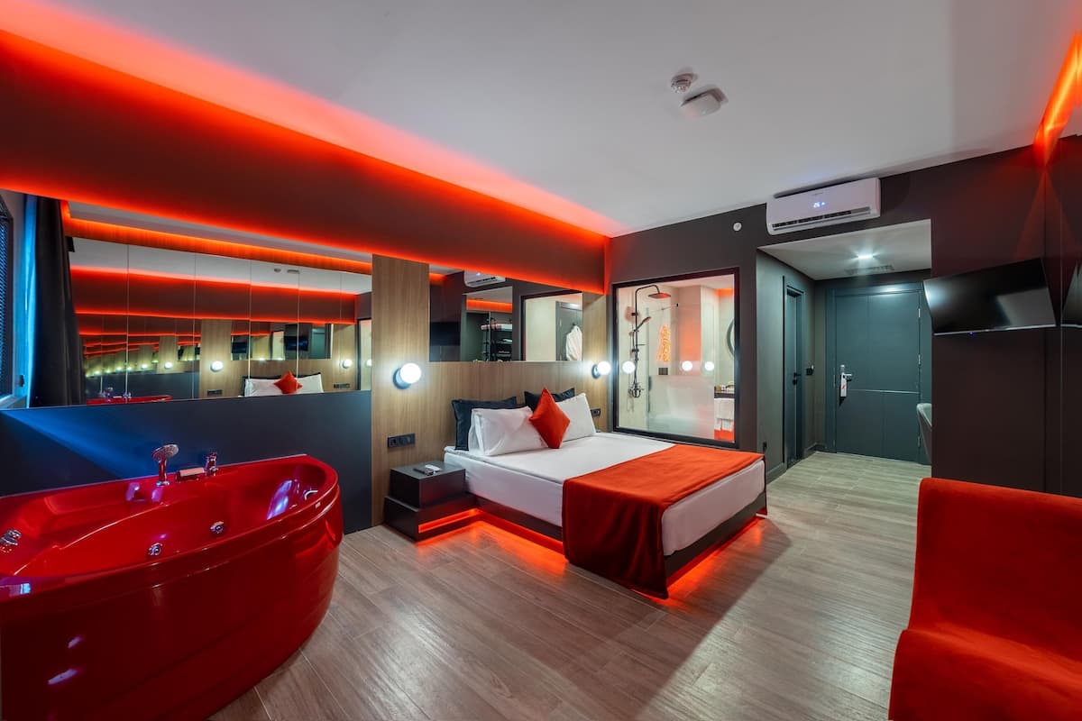 Quarto de hotel moderno com uma cama grande, uma banheira vermelha e um banheiro com chuveiro.