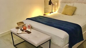 Uma cama bem arrumada com um cobertor azul, um abajur e uma mesinha de cabeceira com um chapéu e óculos de sol.