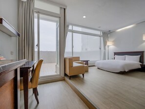 Quarto de hotel com cama, escrivaninha, cadeira e vista através de uma grande janela.