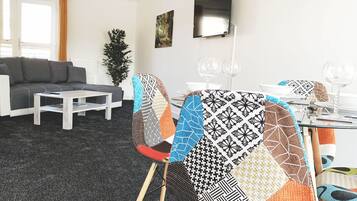 Uma sala moderna com um sofá cinzento, uma mesa de centro e um espaço de jantar com cadeiras estampadas.