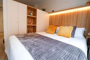 Quarto moderno com uma cama grande, um guarda-roupa de madeira e uma estante com objetos decorativos.