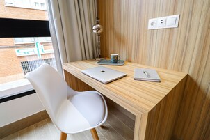 Uma mesa de madeira com um laptop, um caderno e uma xícara. Uma cadeira branca está posicionada em frente à mesa.