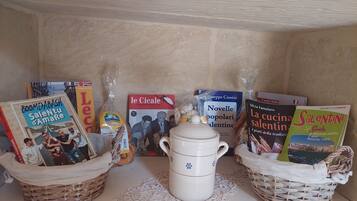 Uma bancada de cozinha com cestos contendo livros, uma garrafa de azeite e um jarro de cerâmica branca.