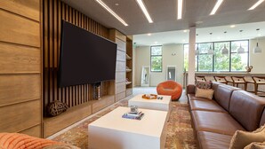 Uma sala de estar moderna com televisão de tela plana, um sofá, duas mesas de centro e um tapete estampado.