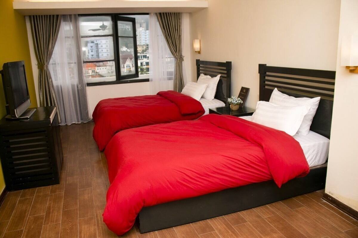 Quarto de hotel com duas camas, televisão e janela com cortinas.