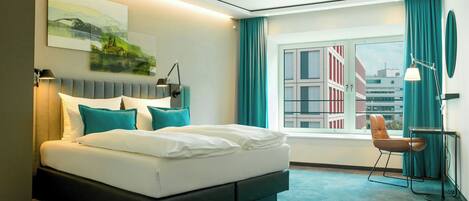 Quarto de hotel moderno com uma cama grande, uma escrivaninha e vista para edifícios pela janela.