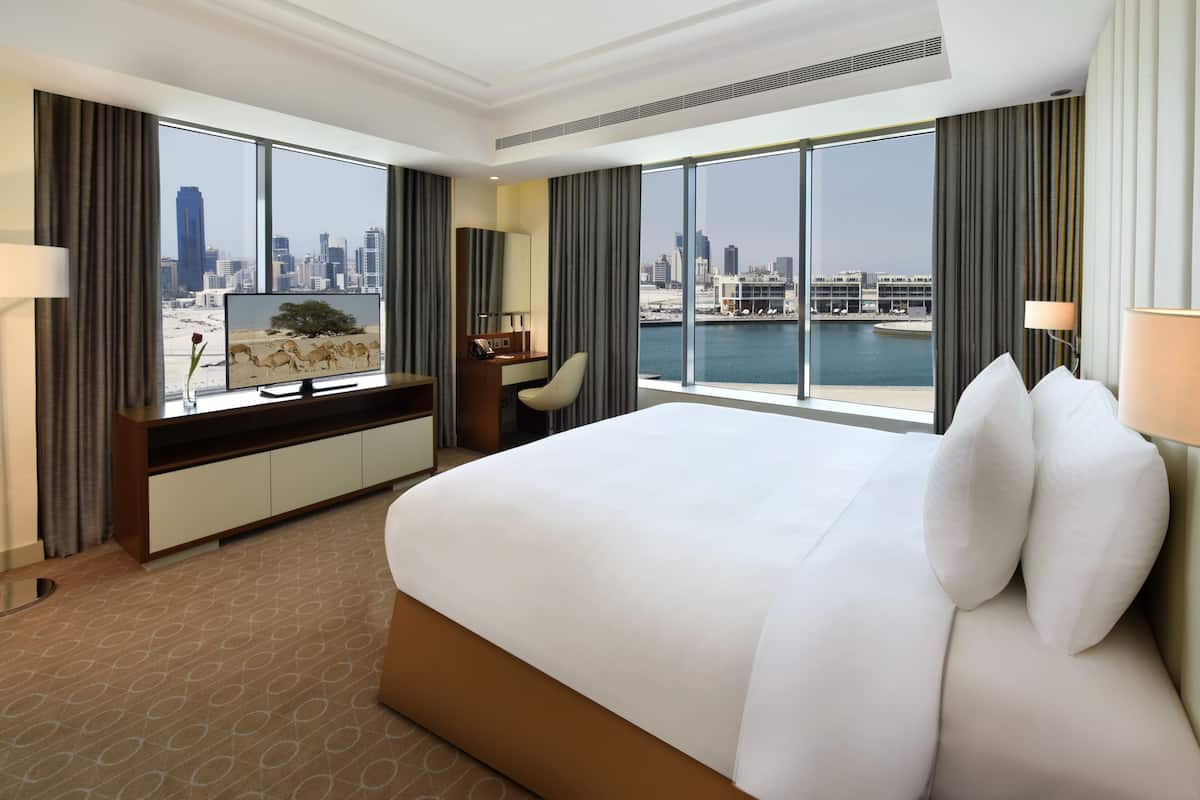 Quarto de hotel com uma cama grande, uma escrivaninha, uma cadeira e vista para a cidade e para a água.