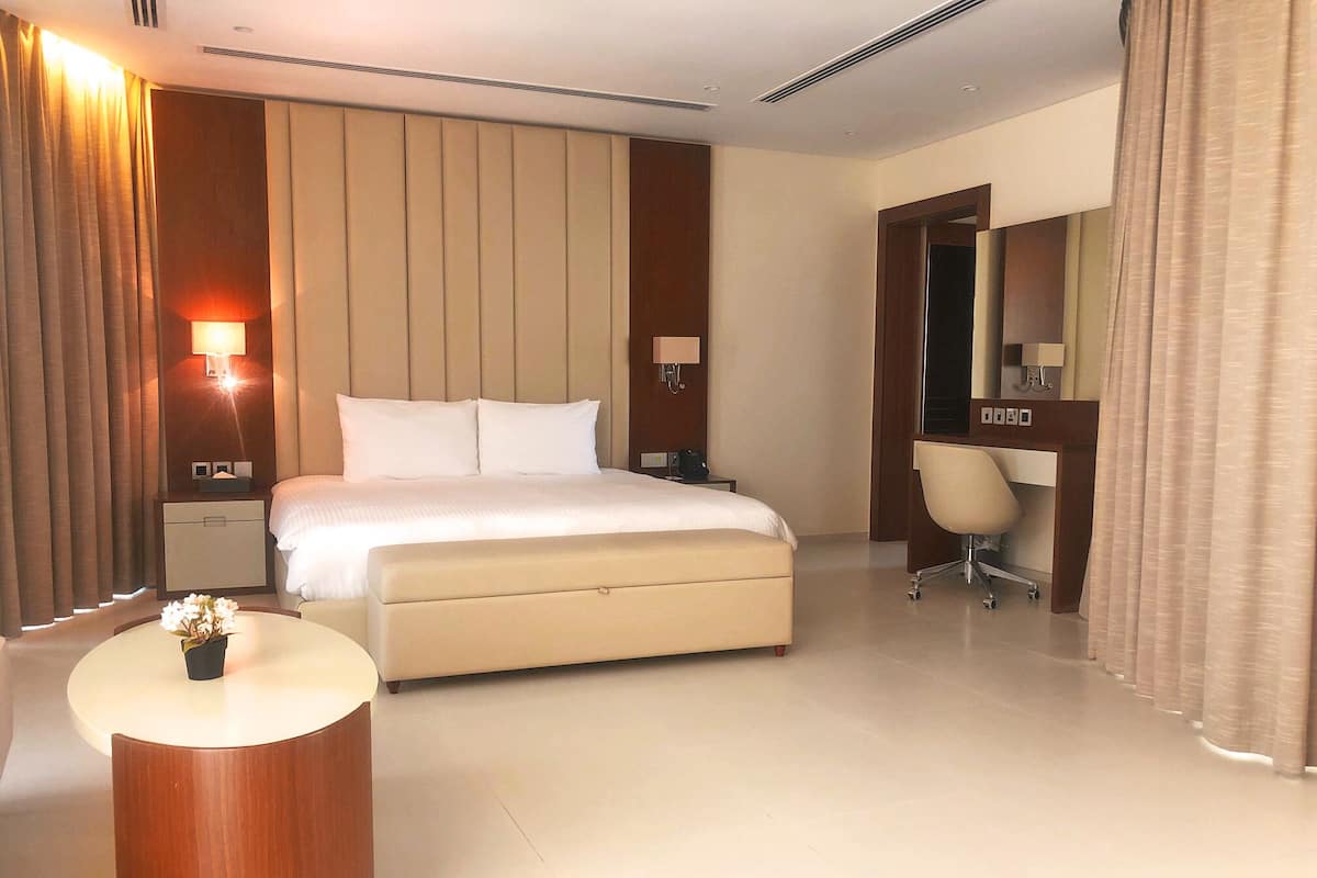 Quarto de hotel com cama grande, escrivaninha, cadeira, mesa redonda e espelho.