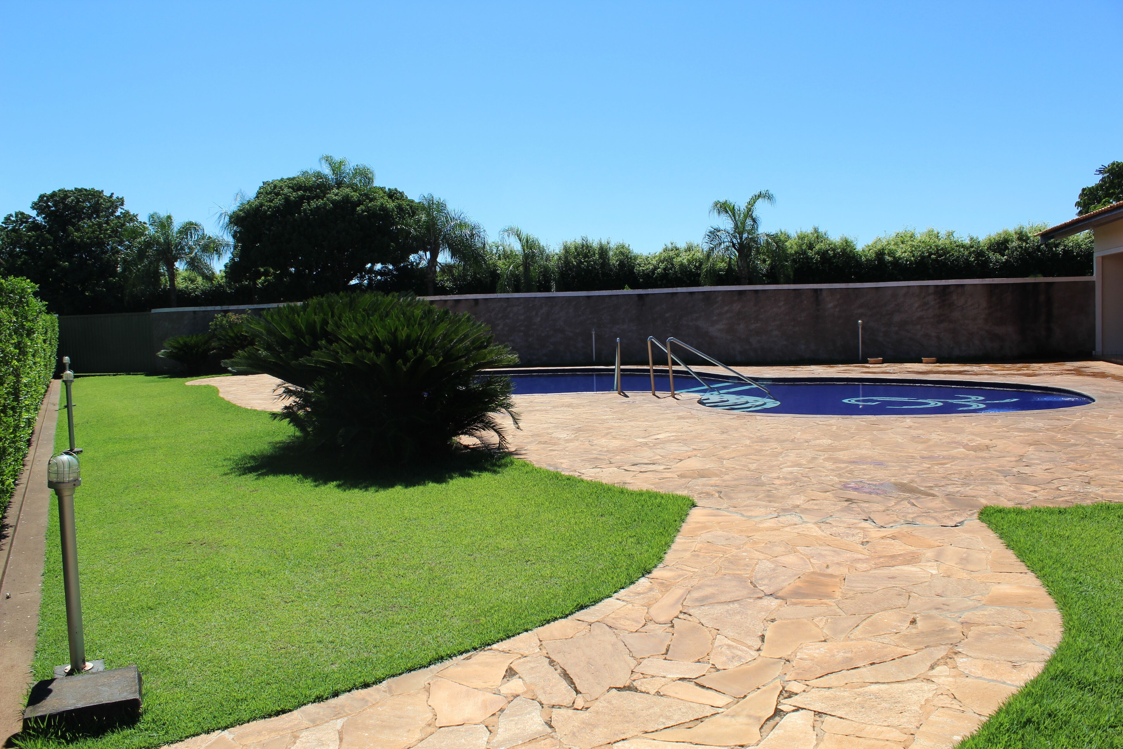 Um quintal com um alpendre de pedra, uma piscina e um gramado bem cuidado.