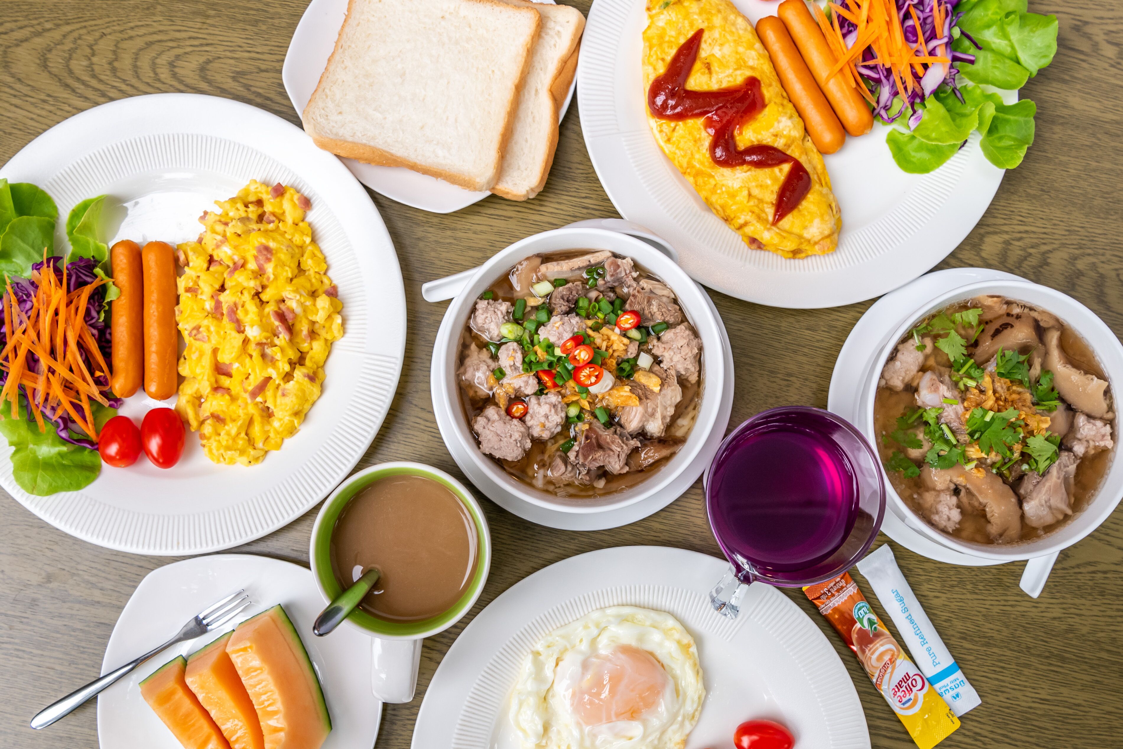 Uma mesa com diversos pratos, incluindo ovos mexidos, salsichas e uma tigela de sopa.