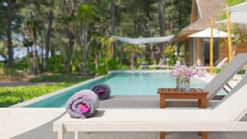 Área da piscina com espreguiçadeiras, uma mesa de madeira com um vaso de flores e uma rede.