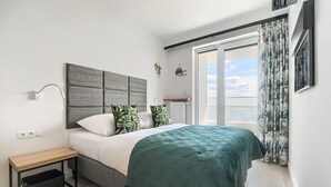Quarto moderno com cabeceira cinzenta, colcha verde e mesa de cabeceira de madeira.