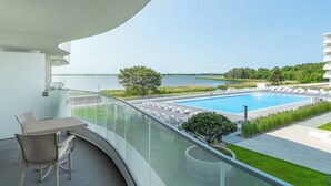 Varanda com guarda-corpo de vidro com vista para uma piscina e um lago.