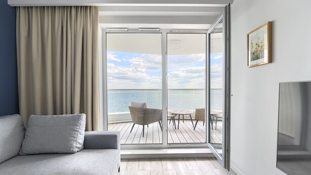 Uma sala de estar moderna com sofá, TV de tela plana e varanda com vista para o mar.