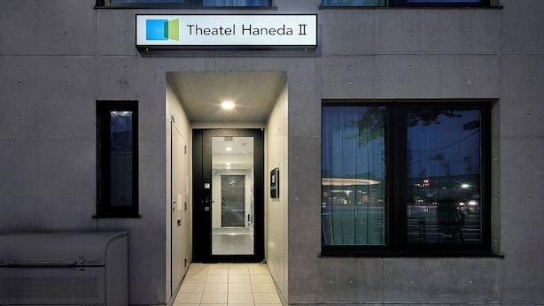 A entrada do Teatro Haneda II, com design moderno, apresenta uma porta de vidro e vista para a rua.