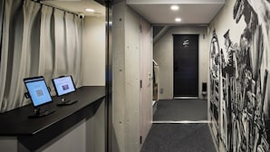 Corredor com porta preta numerada com o número 1, uma câmera de segurança e um código QR em um monitor.