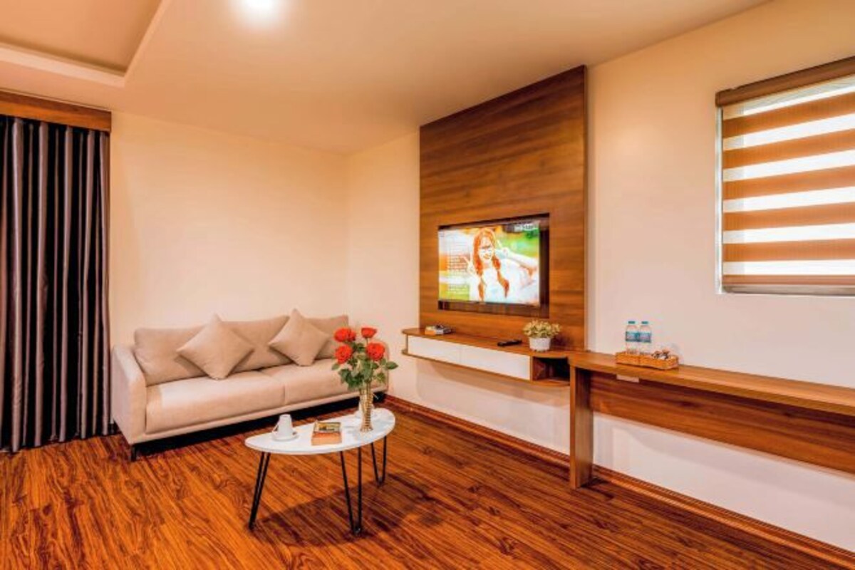 Uma sala de estar moderna com sofá, mesa de centro, TV fixada na parede e janela com persianas.