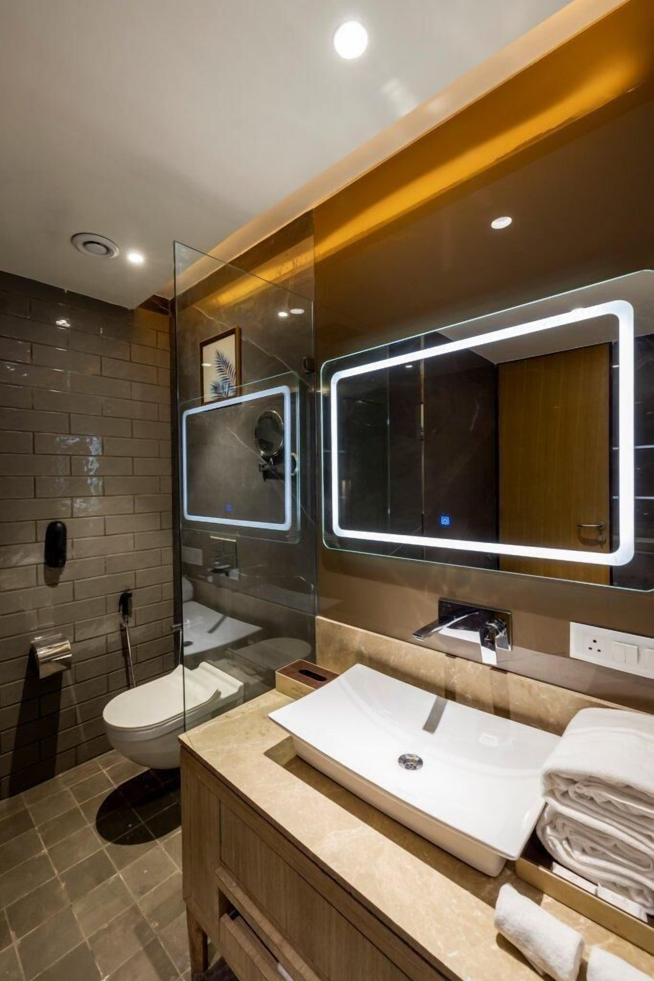 Uma casa de banho moderna com cabine de duche em vidro, toucador com lavatório e espelho grande com iluminação embutida.