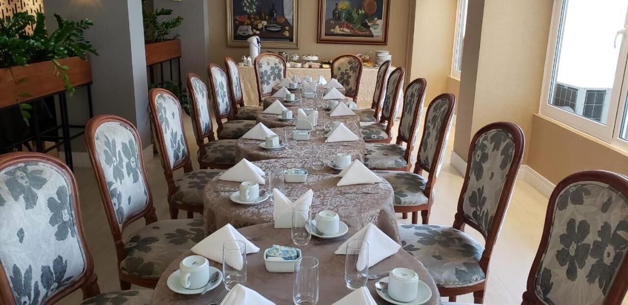 Uma sala de jantar formal com uma mesa comprida posta para uma refeição, rodeada por cadeiras estofadas com estampas florais.