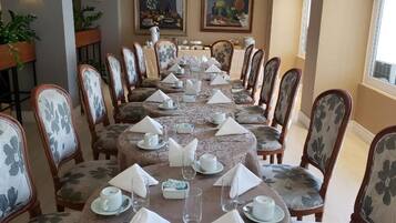 Uma sala de jantar formal com uma mesa comprida posta para uma refeição, rodeada por cadeiras estofadas com estampas florais.