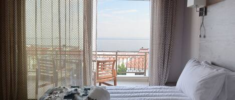 Quarto de hotel com cama, uma cadeira e vista para o mar.