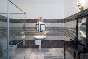 Casa de banho com cabine de duche em vidro, lavatório com espelho e toucador com espelho.