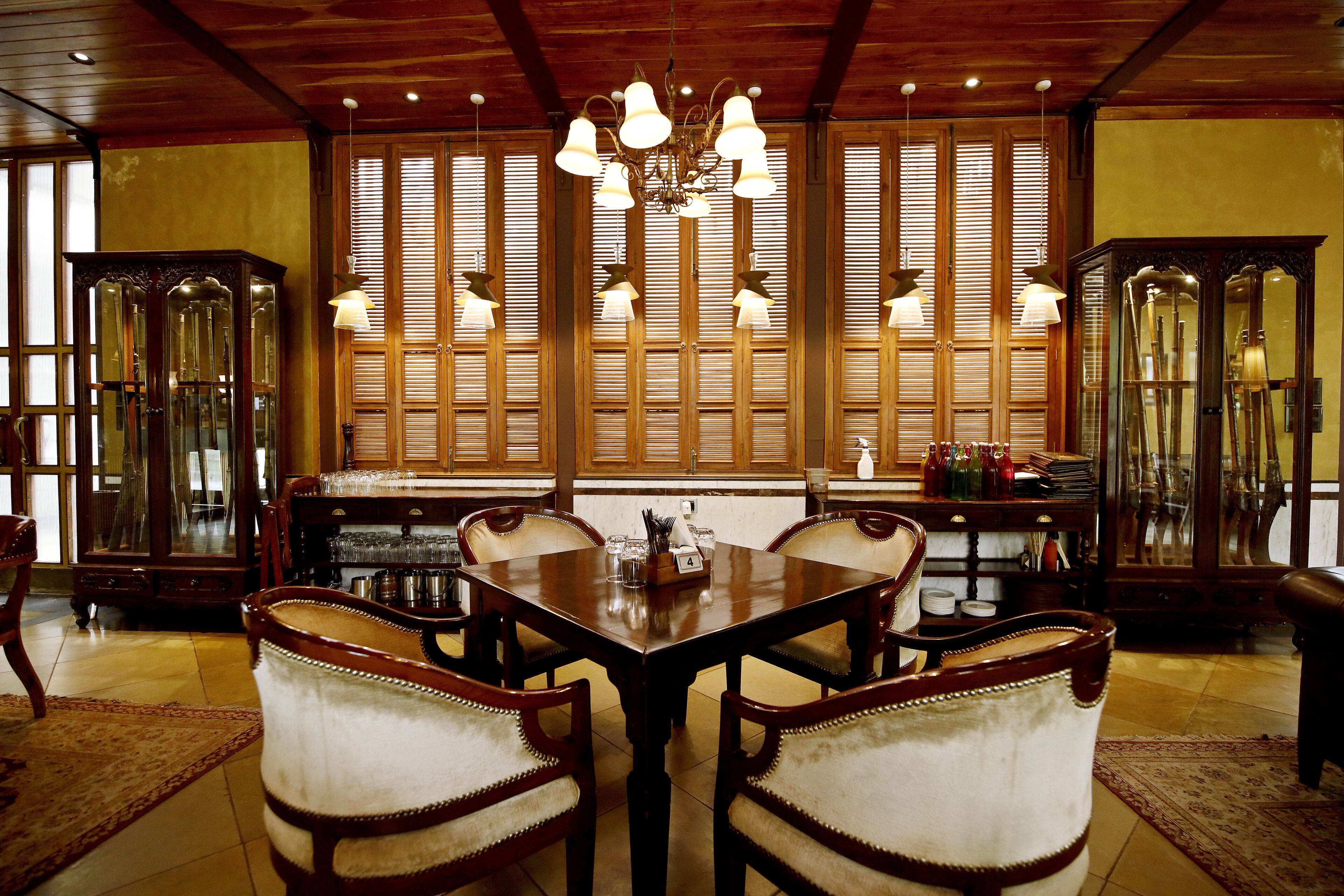 Uma sala de jantar com mesa e cadeiras de madeira, um candelabro e armários de madeira.