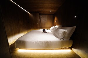 Um quarto pequeno e acolhedor com uma cama de solteiro, um laptop na cama e teto de madeira.