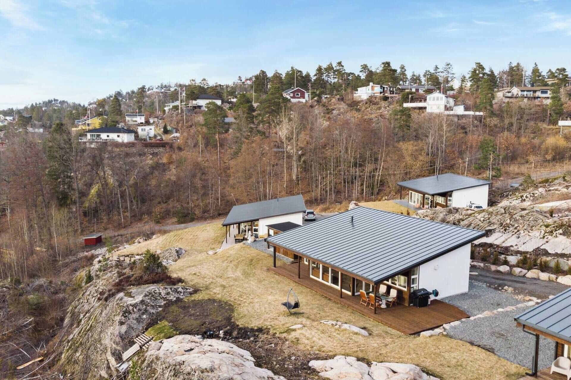 Uma casa moderna com um amplo terraço, cercada por uma paisagem natural com árvores e colinas.