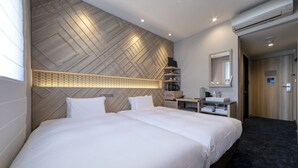Quarto de hotel com duas camas, cabeceira de madeira, uma escrivaninha pequena com espelho e prateleira embutida.