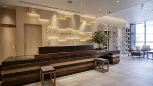Uma área de recepção com design moderno, destacando um balcão de madeira, uma parede texturizada e uma grande janela que oferece iluminação natural.