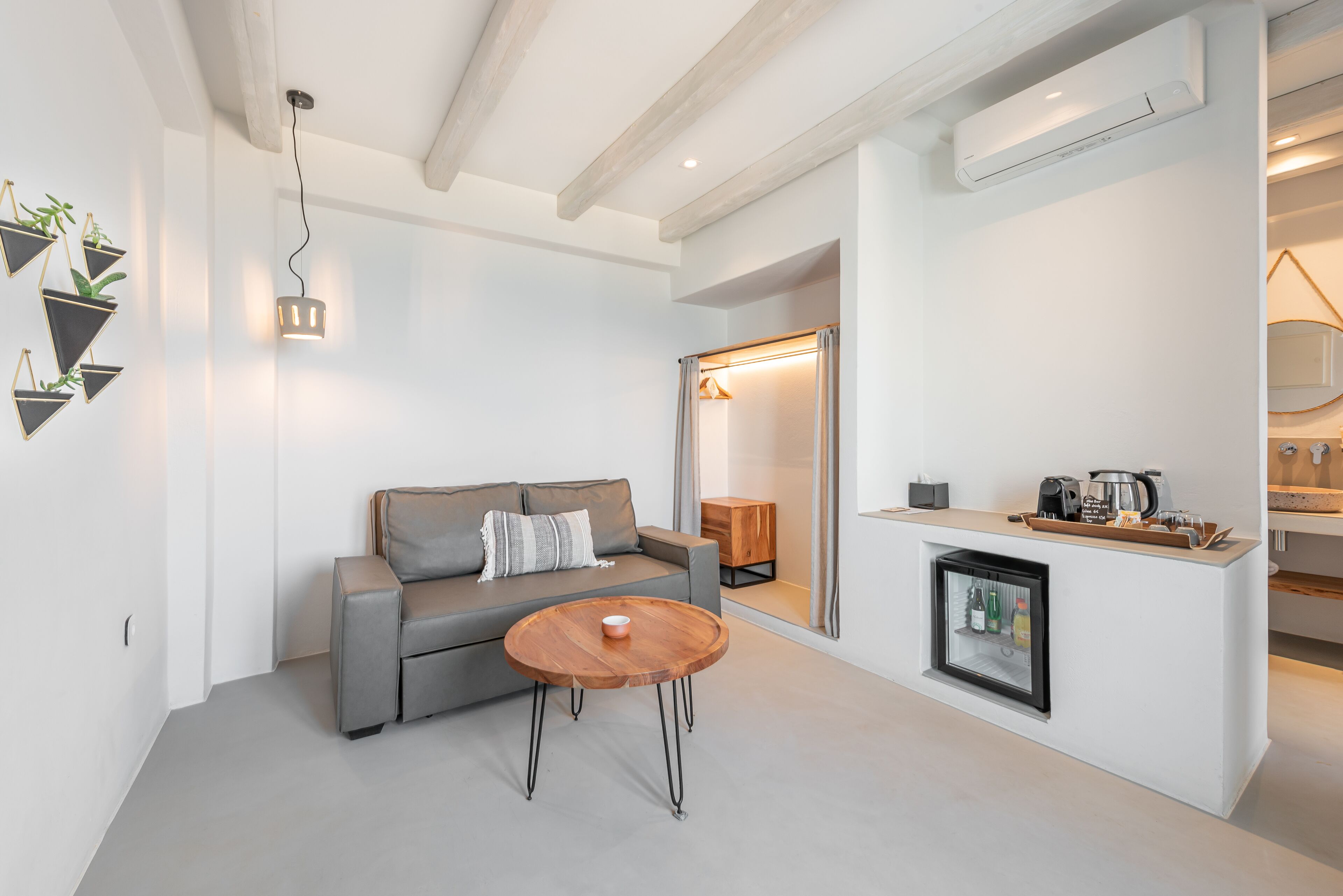 Uma sala de estar moderna com um sofá cinzento, uma mesa de centro de madeira e um mini-frigorífico embutido.