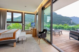Quarto com cama grande, escrivaninha, cadeira e varanda com vista para montanhas e vegetação.