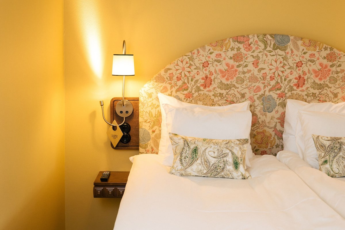 Quarto com cama, mesa de cabeceira, abajur e cabeceira com padrão floral.
