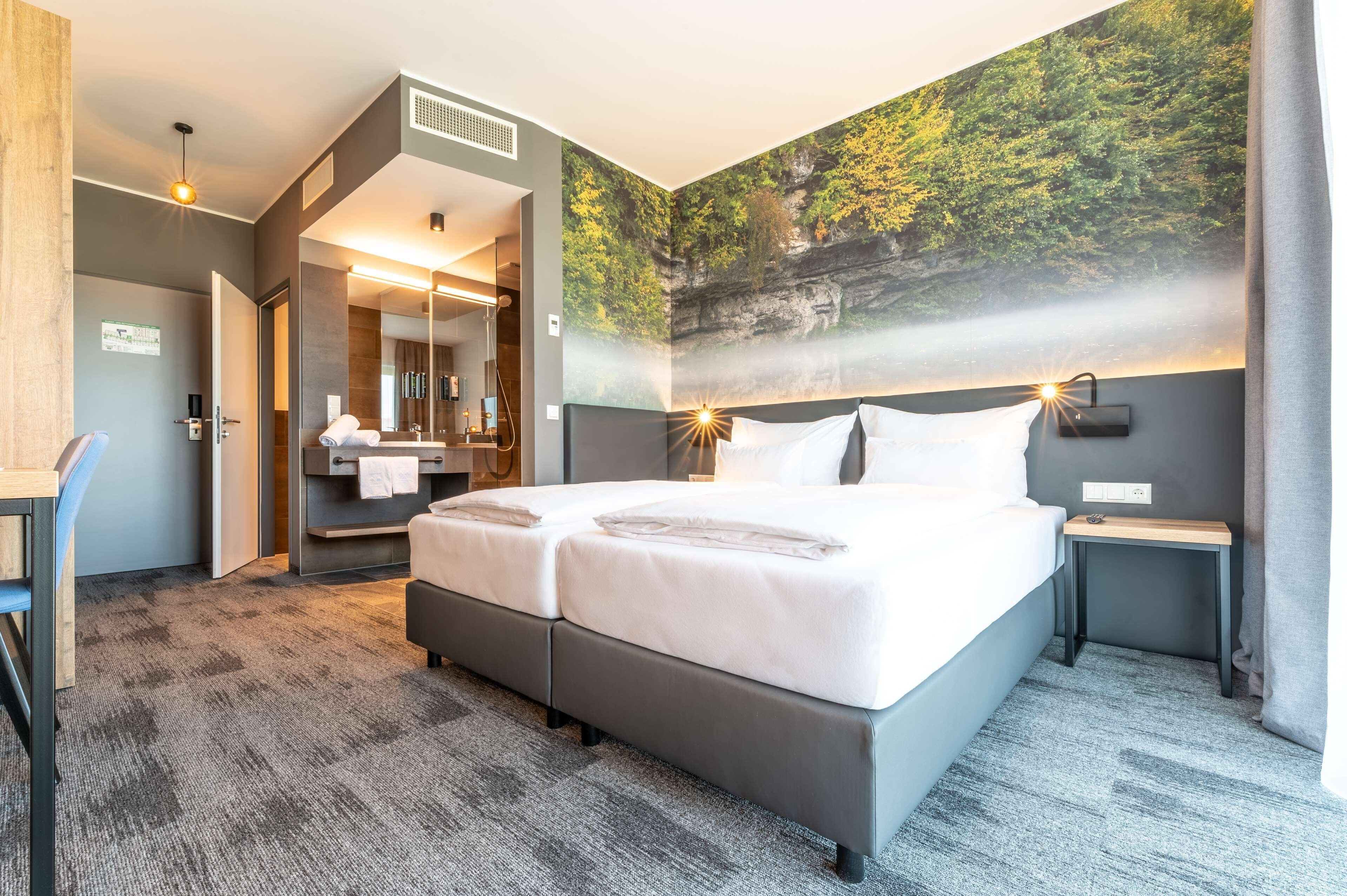 Quarto de hotel moderno com uma cama grande, uma escrivaninha, um espelho e um mural na parede.