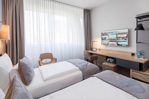 Quarto de hotel com cama, escrivaninha, cadeira e televisão exibindo um cardápio.