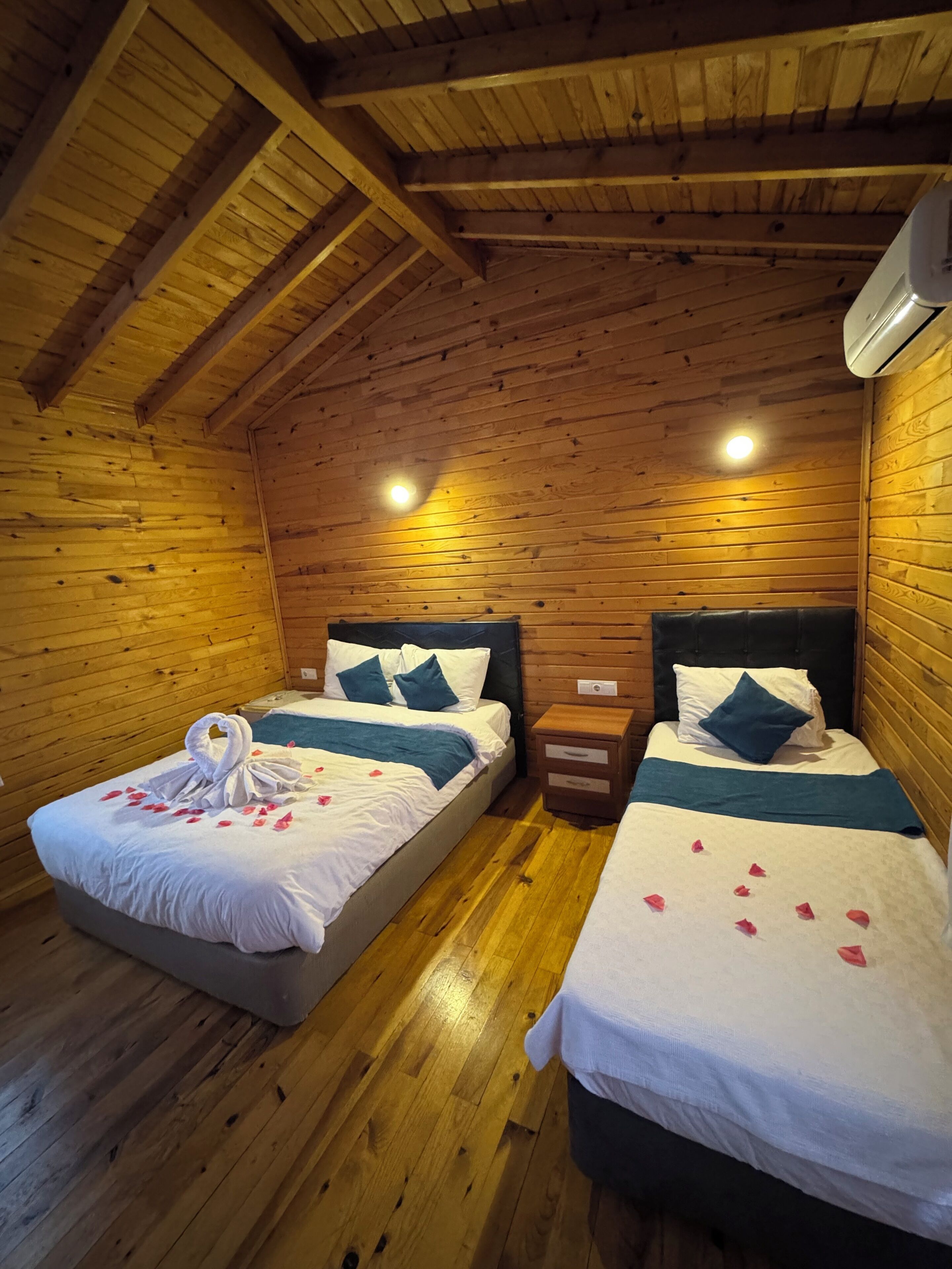 Quarto de cabana de madeira com duas camas, cada uma com cabeceira, mesas de cabeceira e ar condicionado fixado na parede.