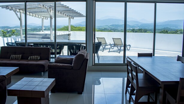 Uma sala de estar moderna com uma grande porta de vidro que dá para uma varanda com vista para as montanhas.