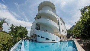 Um edifício moderno, com vários andares e um design curvo característico, ao lado de uma piscina.