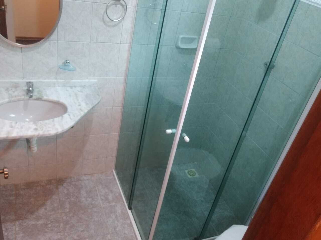 Casa de banho com lavatório de mármore, cabine de duche em vidro e sanita.