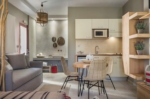 Um espaço de estar compacto com sofá, mesa de jantar, cadeiras, área de cozinha com armários e micro-ondas, e luminária pendente.