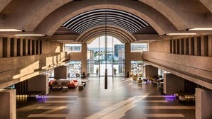 Um hall amplo com teto alto e design em arco, apresentando uma área central aberta com assentos e vista para a paisagem urbana.