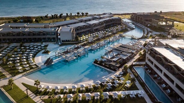 Um resort com uma grande piscina central, vários quartos de hóspedes e vista para o oceano.