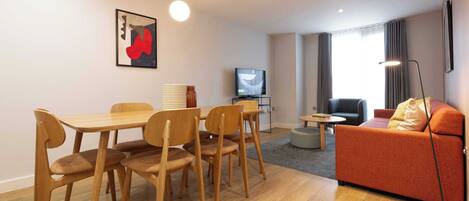 Uma sala de estar moderna com área de jantar, sofá, televisão e um quadro na parede.