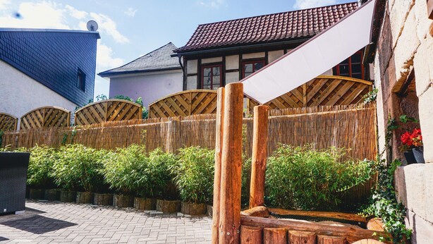 Pátio com cerca de madeira, plantas de bambu e muro de pedra.