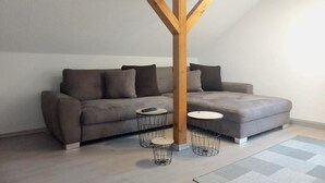 Uma sala de estar moderna com um sofá cinza, duas mesinhas redondas e um teto de madeira.